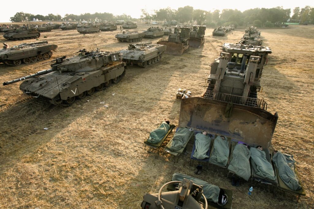 Israeli soldiers sleep next to armored vehicles at a gathering point ...